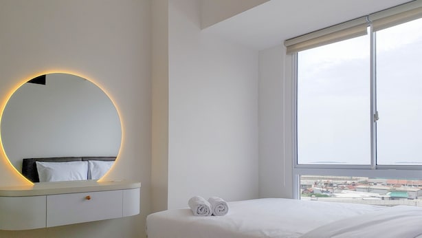 Quarto de hotel moderno com uma cama grande, um espelho redondo com iluminação na borda, uma mesinha de cabeceira e uma janela com vista para a cidade.