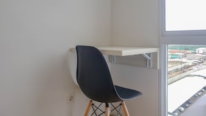 Quarto de canto com uma cadeira preta, uma prateleira de madeira e uma janela vista para a cidade.