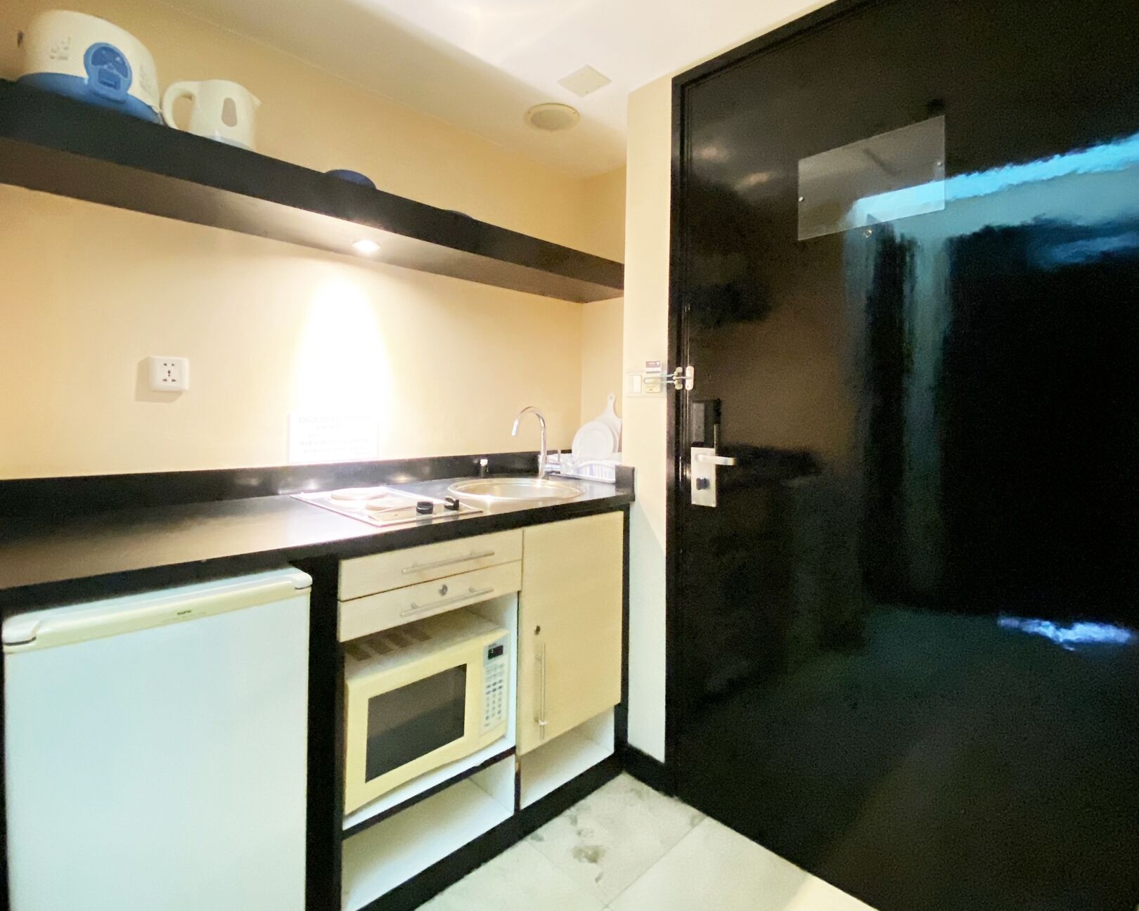 Uma cozinha compacta com micro-ondas, pia e uma porta com moldura preta.
