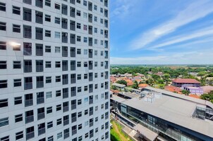 Um edifício alto com uma fachada de janelas e varandas, e vista para uma cidade com diversos edifícios e áreas verdes.