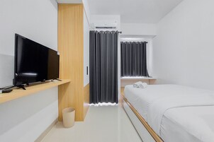 Quarto de hotel moderno com televisão de tela plana em prateleira de madeira, cama com roupa de cama branca e pequena mesa de cabeceira.