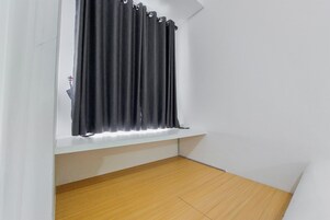 Quarto com janela, paredes brancas e chão de madeira.