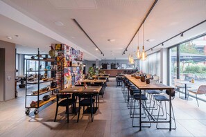 Interior moderno de café com pé-direito alto, dutos aparentes e diversas opções de assento, incluindo mesas e banquetas.