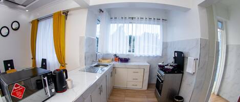 Cozinha compacta com micro-ondas, cafeteira e pia. Há uma janela com cortinas e vista para o exterior.