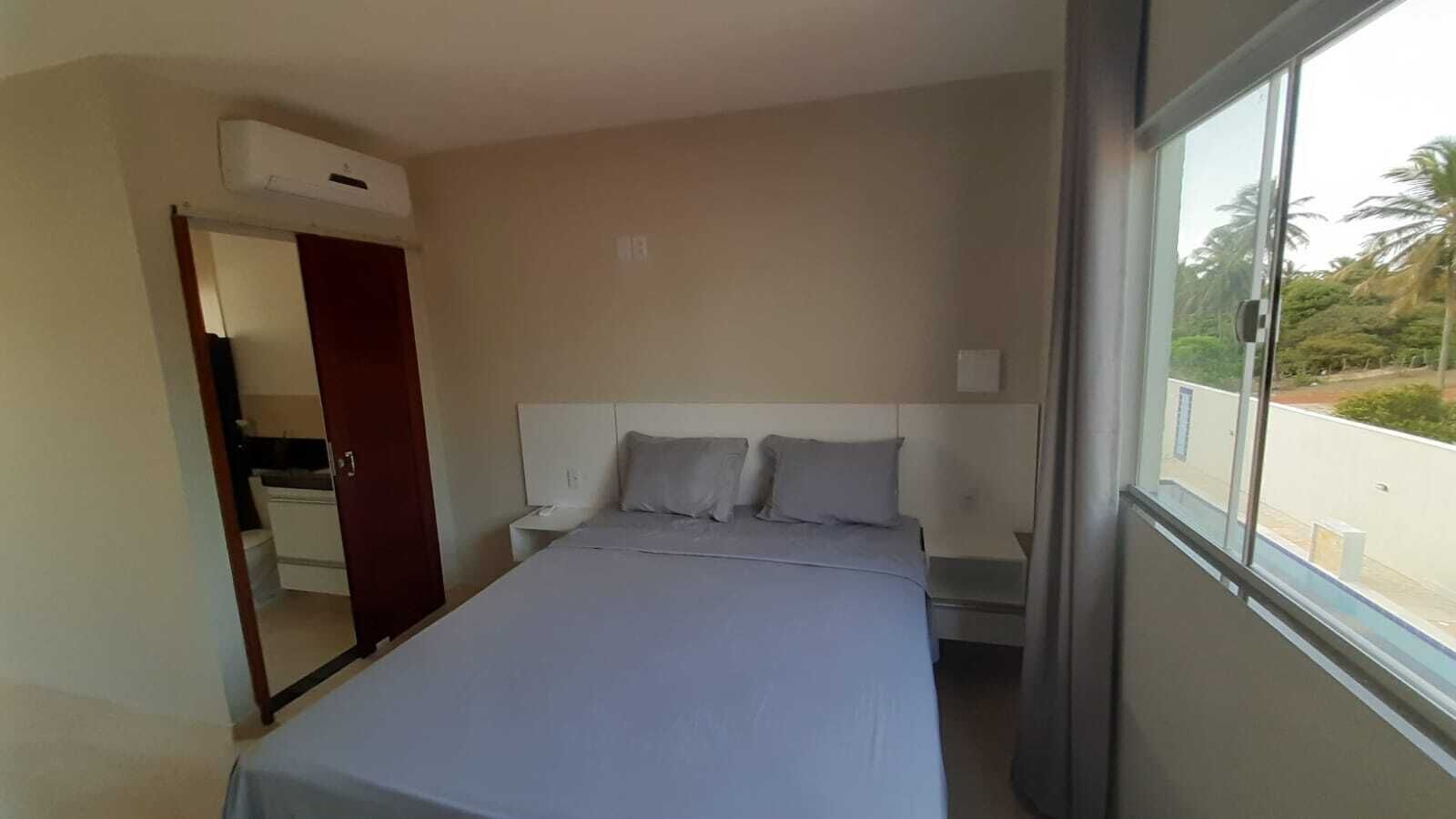 Quarto de hotel com uma cama, uma mesa de cabeceira, uma janela e uma porta para um banheiro.