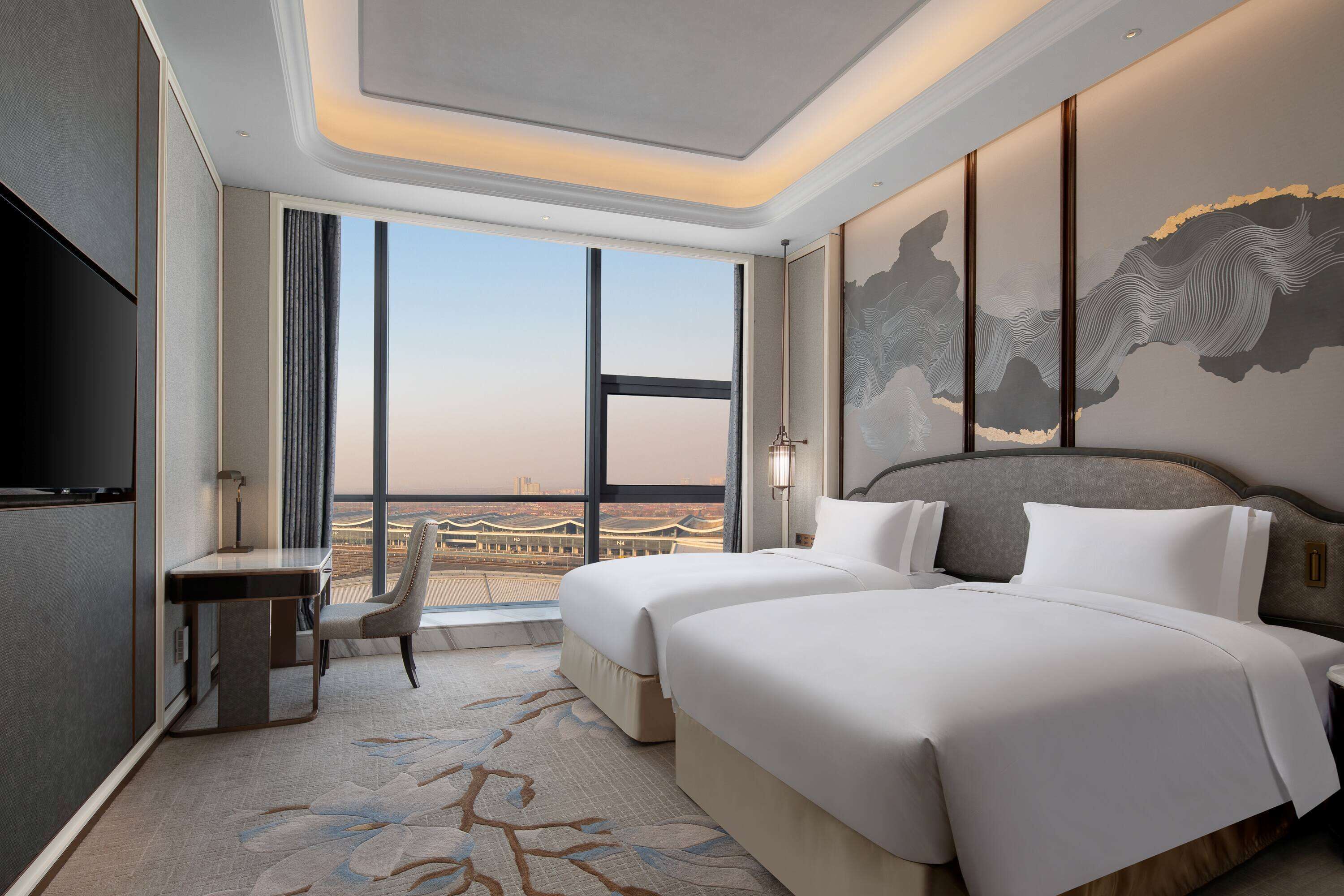 Quarto de hotel com uma cama grande, uma escrivaninha e uma televisão.