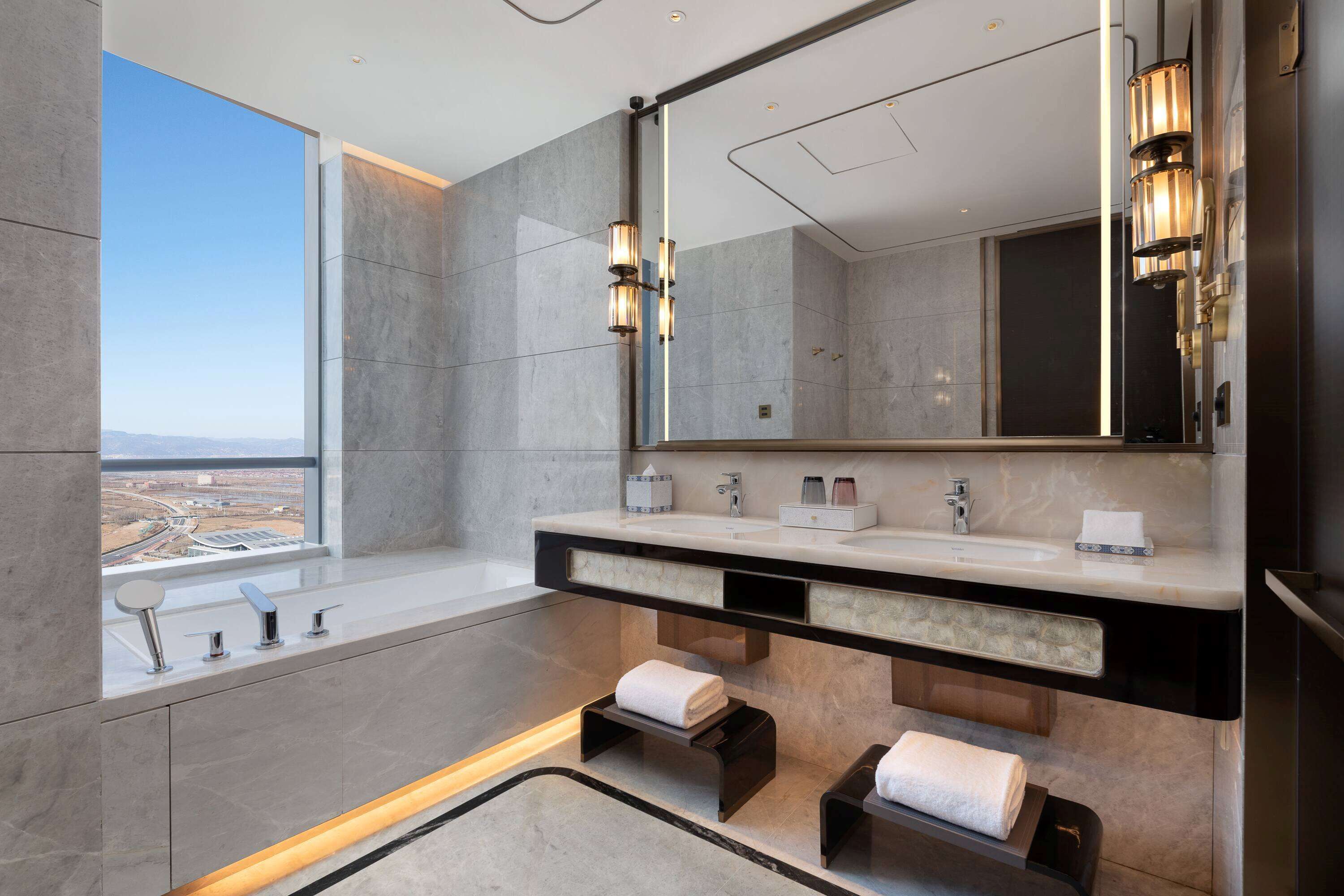 Uma casa de banho moderna com um espelho grande, duas pias, uma banheira e vista para a cidade.