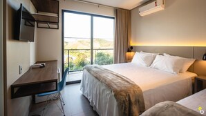 Quarto de hotel com cama, escrivaninha e uma grande janela.