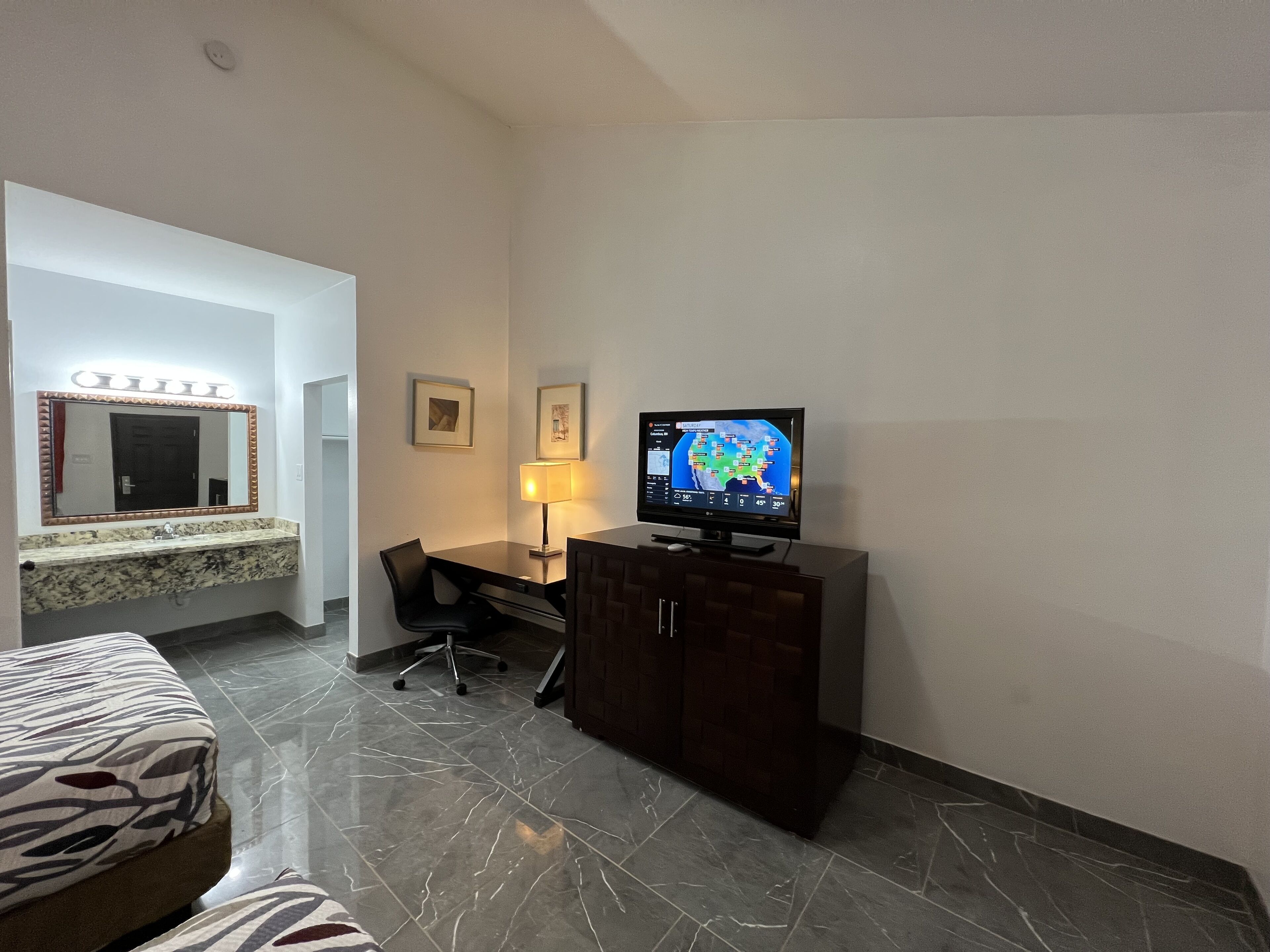 Quarto de hotel com cama, escrivaninha com cadeira, televisão, espelho e armário.