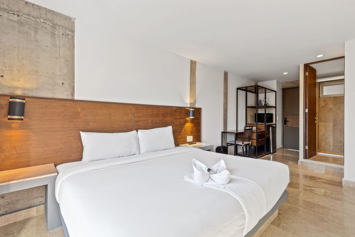 Quarto de hotel moderno com uma cama grande, cabeceira de madeira e uma pequena escrivaninha com uma cadeira.