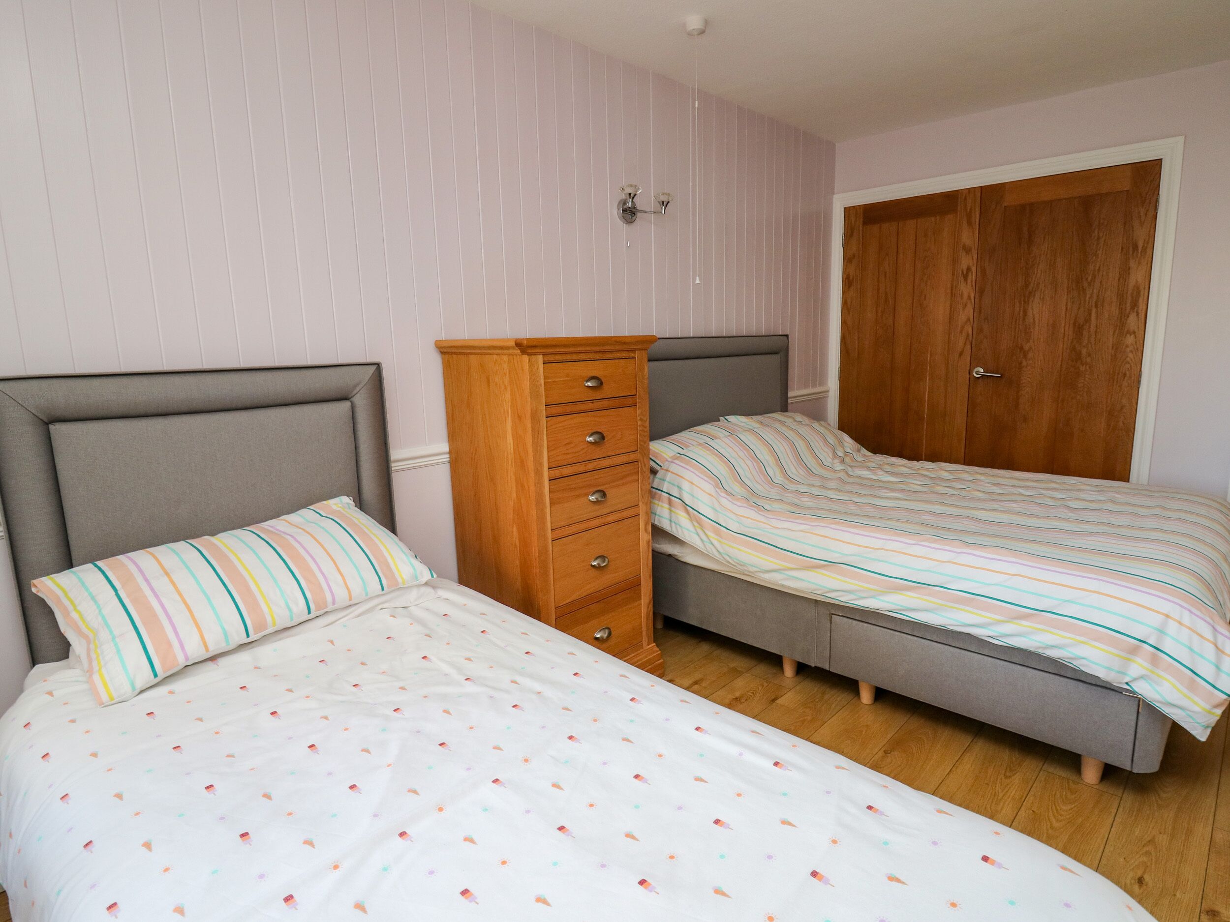 Quarto com duas camas de solteiro, cômoda de madeira e guarda-roupa.