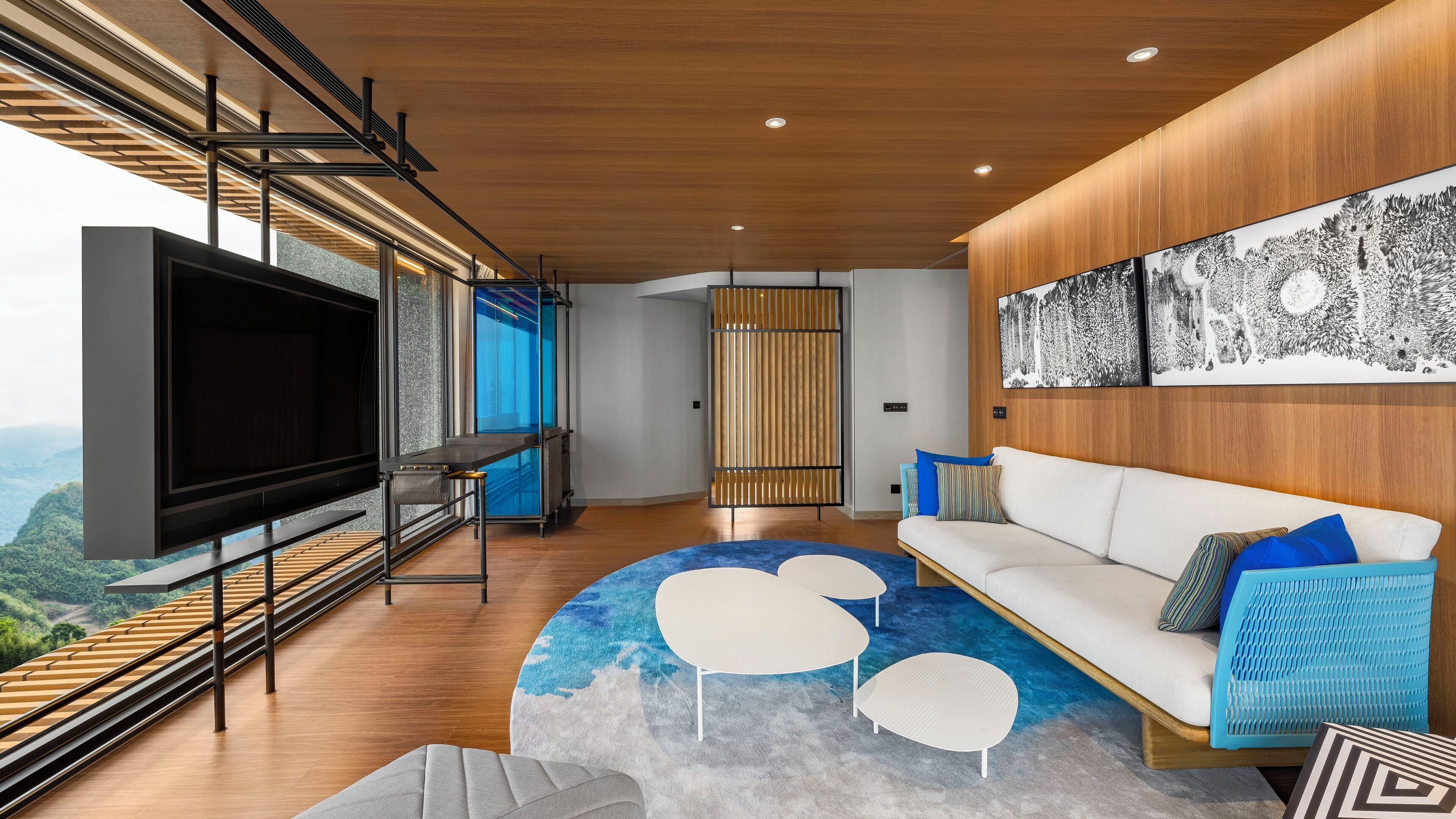 Uma sala de estar moderna com uma televisão grande, um sofá, uma mesa de centro e vista para o exterior.