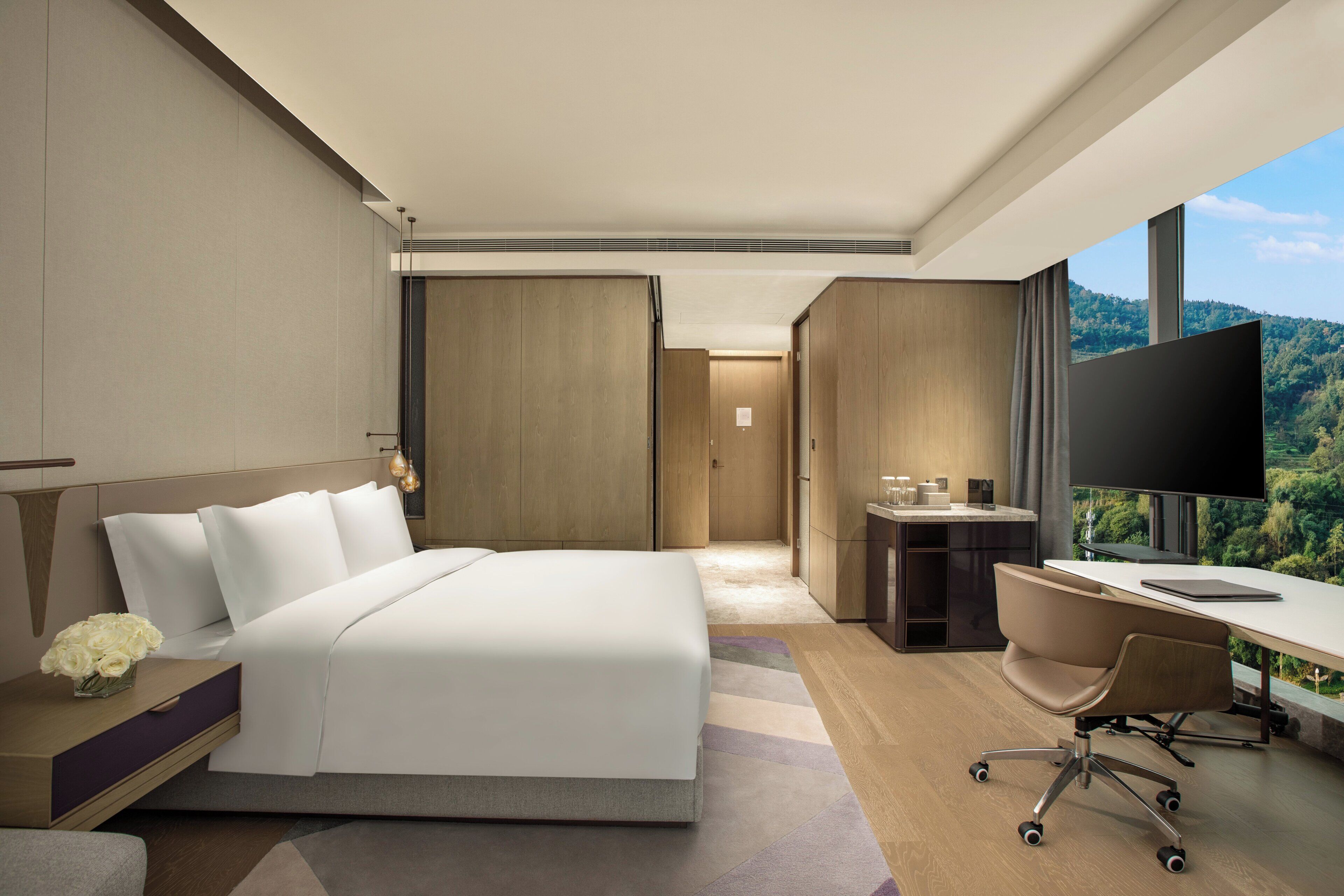 Quarto de hotel moderno com cama grande, escrivaninha e televisão.