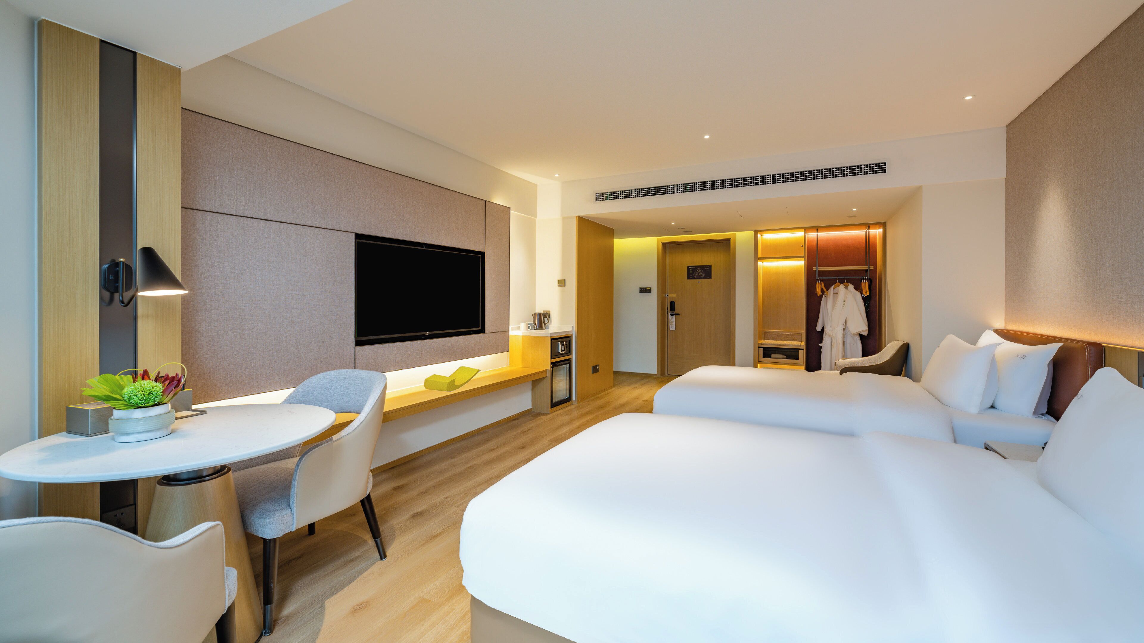 Quarto de hotel com cama, escrivaninha, cadeira, televisão e roupão pendurado na parede.