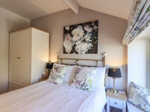 Quarto com cama, mesa de cabeceira, abajur, guarda-roupa e um quadro de flores na parede.
