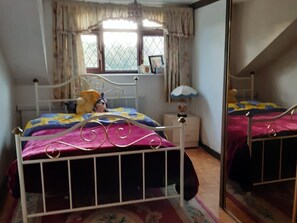 Quarto com estrutura de cama em metal, janela com cortinas, abajur e espelho.