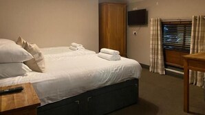 Quarto de hotel com cama, guarda-roupa de madeira, televisão na parede e janela com cortinas.