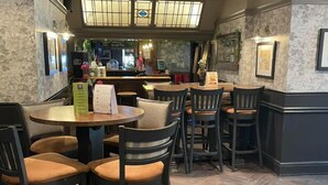 Um restaurante com área de bar, piso de madeira e teto alto com iluminação embutida.