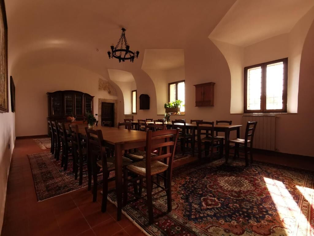 Uma sala de jantar espaçosa com várias mesas e cadeiras de madeira, um candelabro e um tapete grande com padrão.