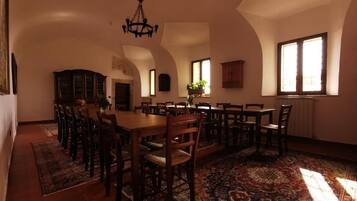 Uma sala de jantar espaçosa com várias mesas e cadeiras de madeira, um candelabro e um tapete grande com padrão.