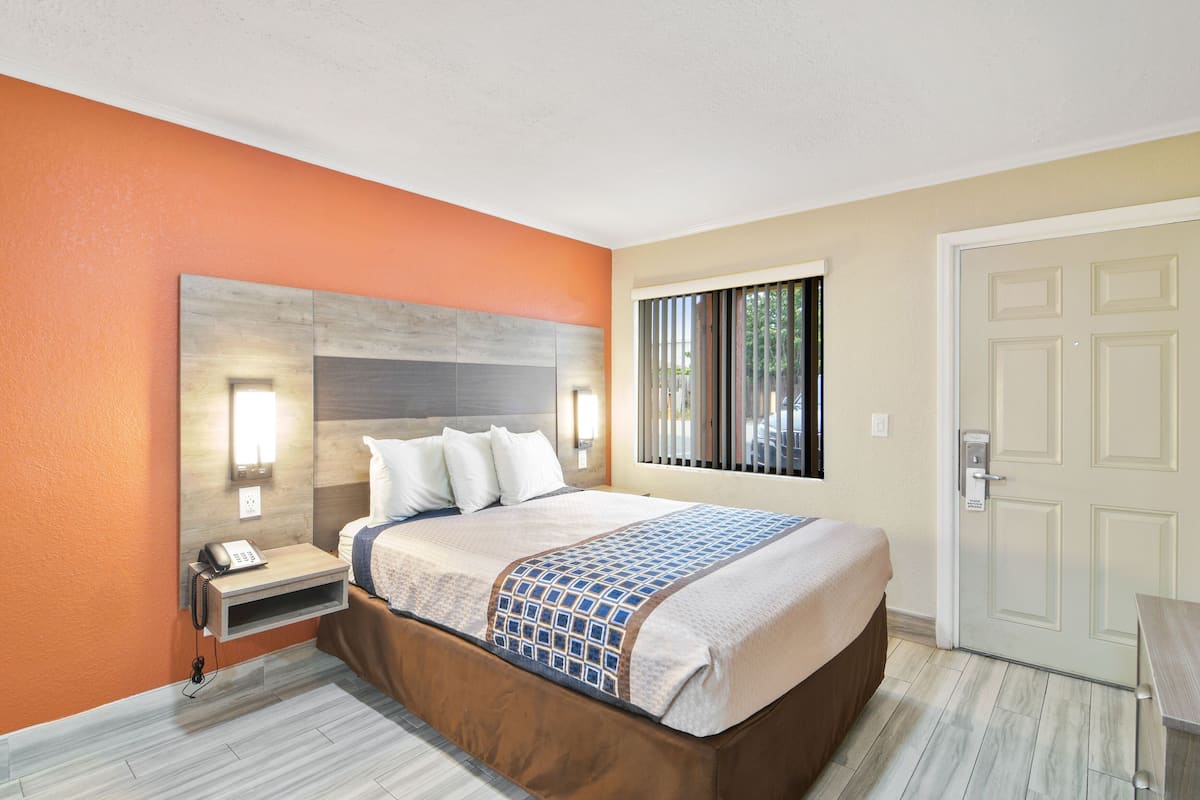 Quarto de hotel com uma cama grande, telefone ao lado da cama, janela com persianas e uma porta.