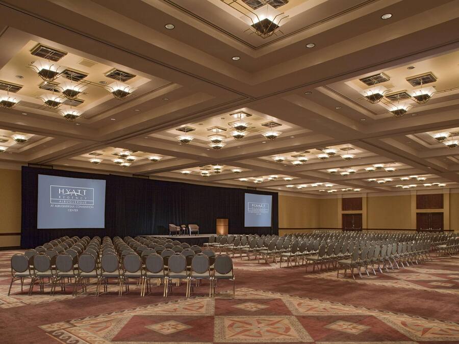 Uma grande sala de conferências com fileiras de cadeiras, um palco e uma tela grande exibindo 'Hyatt Regency'.