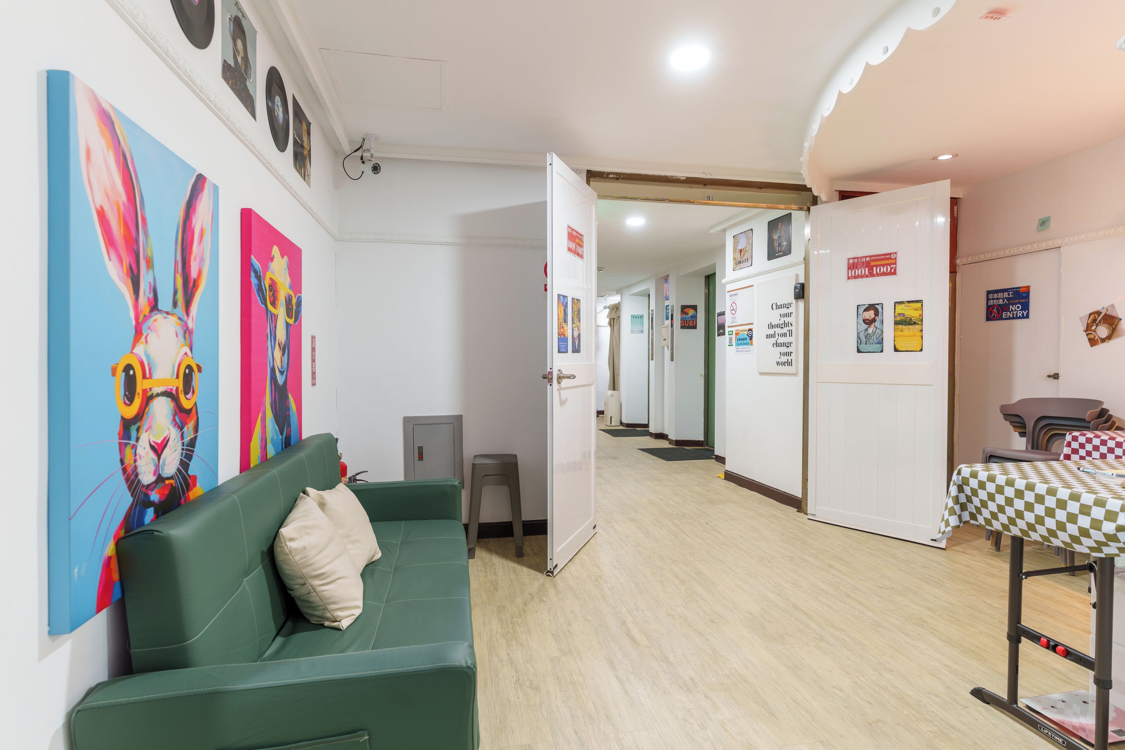Um saguão de hotel com um sofá verde, uma mesa com toalha xadrez e obras de arte coloridas nas paredes.