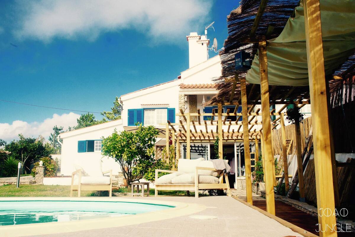 Uma casa com piscina, pérgola de madeira e estrutura de telhado de palha.