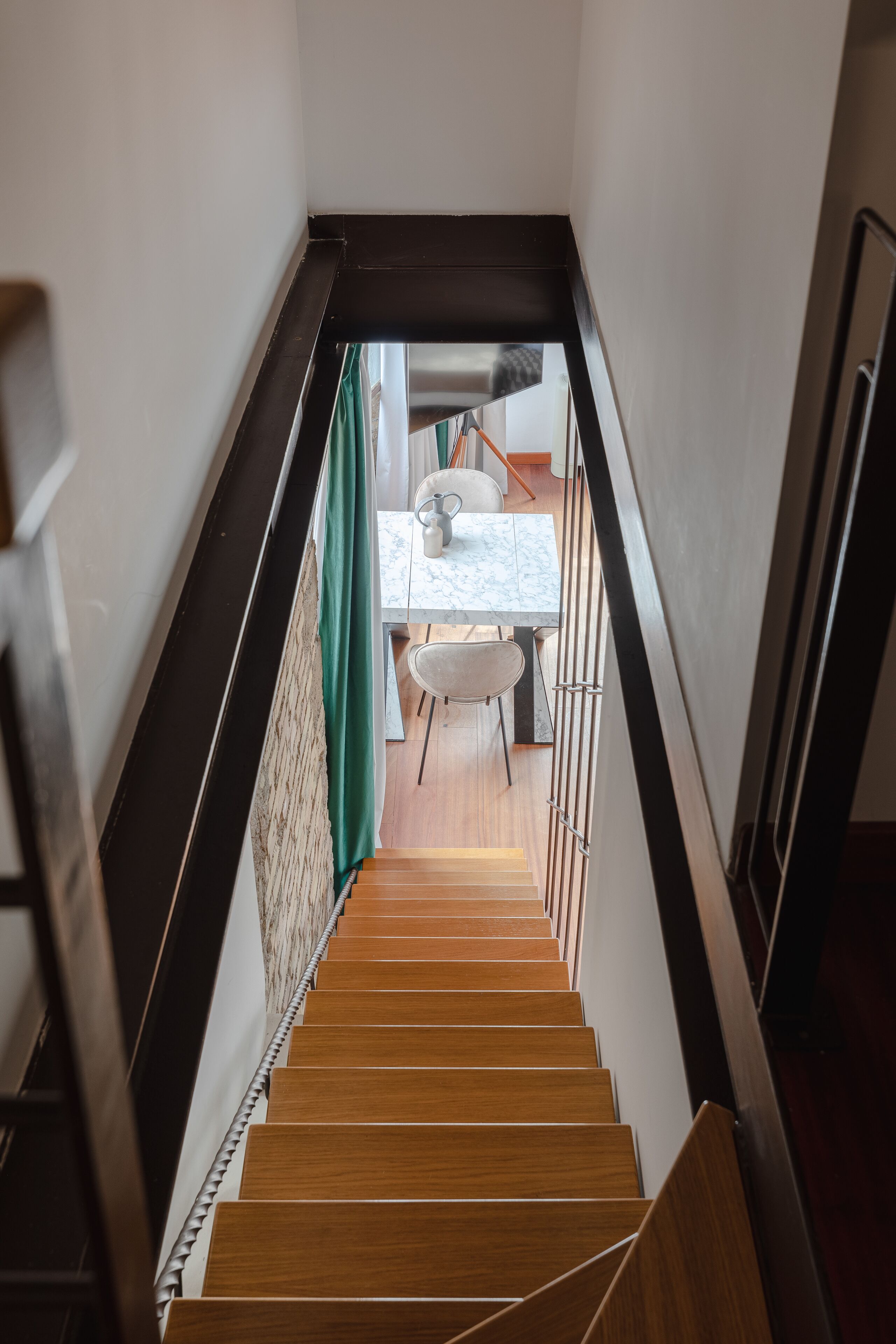 Escada de madeira que dá acesso a uma sala de jantar com mesa e cadeiras.
