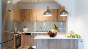 Uma cozinha moderna com armários de madeira, eletrodomésticos de aço inoxidável, bancada branca e iluminação pendente.