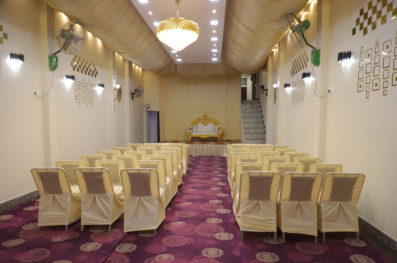 Uma sala de conferências com fileiras de cadeiras, palco com fundo dourado e carpete estampado.