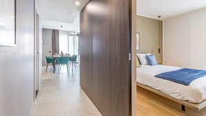 Quarto de hotel moderno com uma cama grande, um armário de madeira, área de refeições com cadeiras e vista para o refeitório.