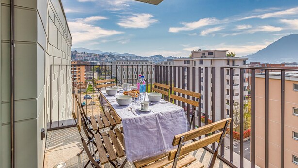 Varanda com mesa posta para refeições, com vista para paisagem urbana, edifícios e montanha.