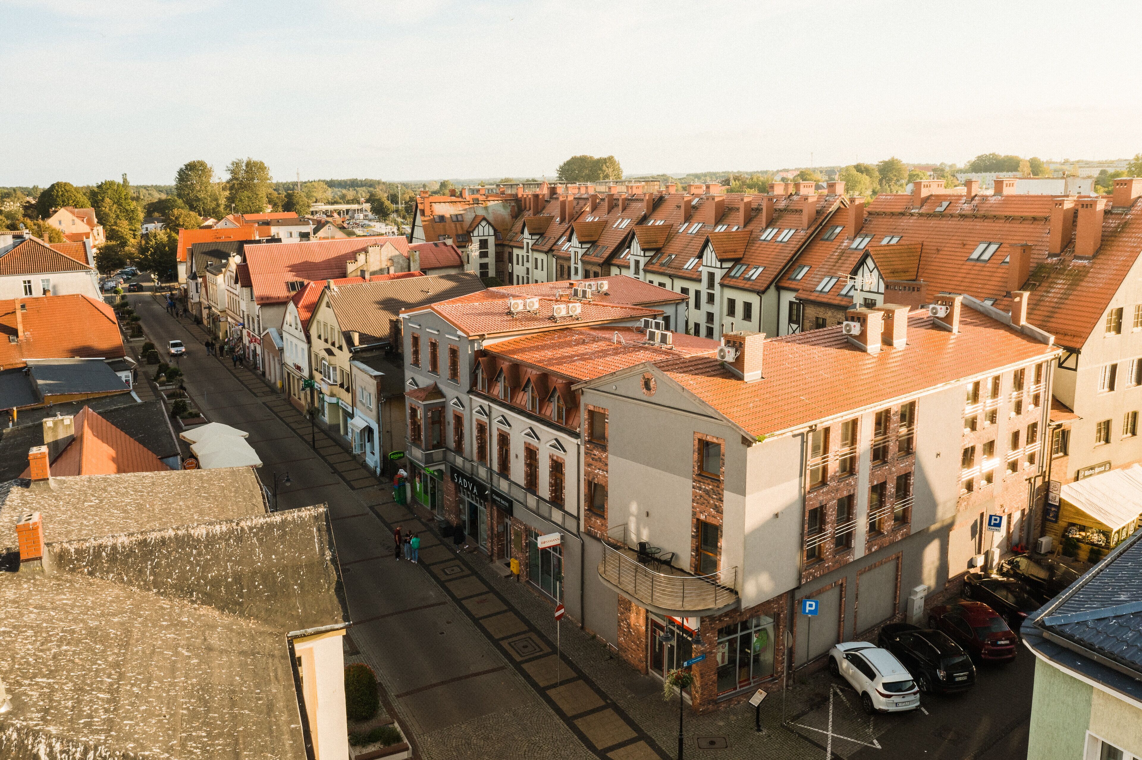 Vista da rua de uma cidade com edifícios tradicionais, céu limpo e carros estacionados.