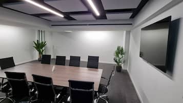 Uma sala de conferências com uma mesa comprida, cadeiras pretas e plantas em vasos.