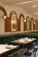 Um restaurante com área de assentos em cabines estofadas de verde, mesas de madeira e arandelas na parede.