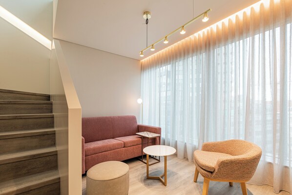 Uma sala de estar moderna com escada, sofá, mesa redonda e uma cadeira.