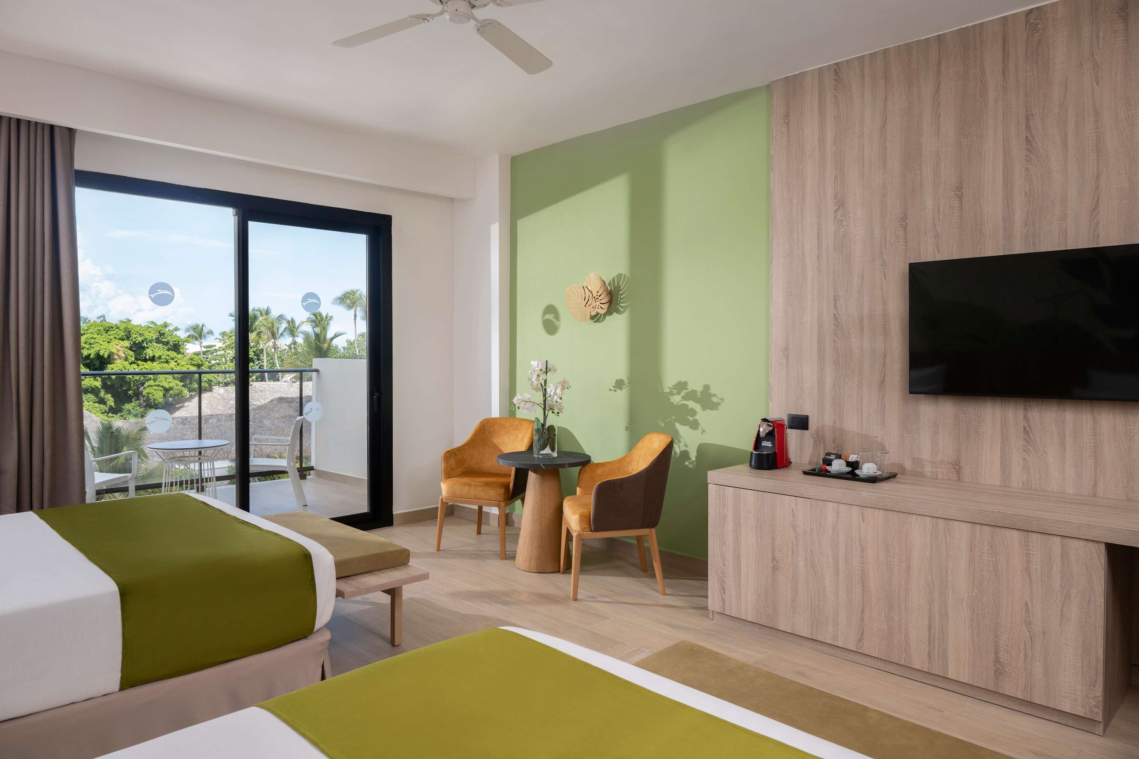 Quarto de hotel com duas camas, televisão, mesa com cafeteira e varanda com mesa e cadeiras.