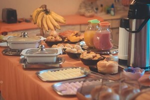 Uma mesa de buffet com diversos alimentos e acompanhamentos, incluindo um termo, uma saladeira e uma garrafa de suco.