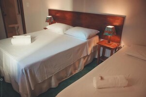 Quarto de hotel com uma cama de casal, uma cama simples e duas luminárias de cabeceira.