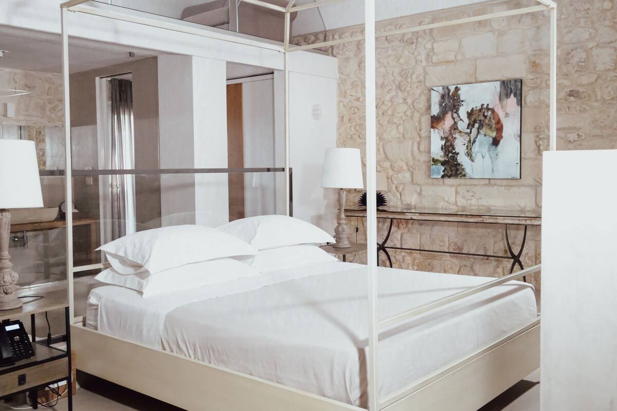 Quarto moderno com cama de dossel, banheiro com chuveiro e parede de pedra com obras de arte.