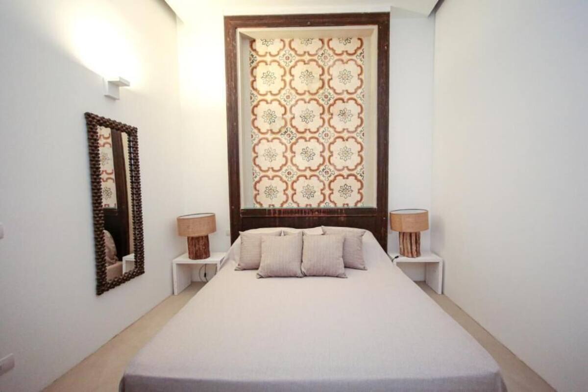 Quarto bem arrumado com uma cama grande, duas mesas de cabeceira, um espelho e um painel de parede estampado.