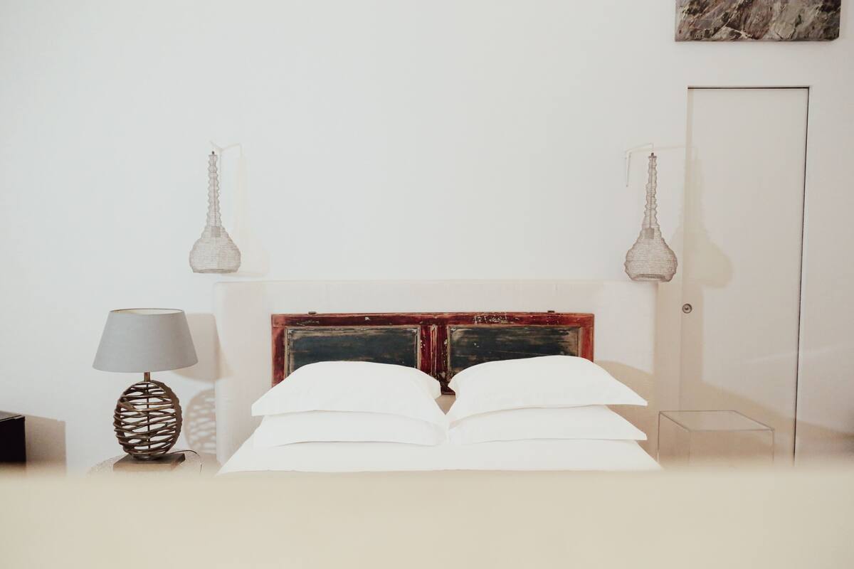 Um quarto com uma cama, uma mesa de cabeceira com abajur e uma porta.