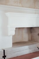 Lareira branca com base de pedra, instalada em um quarto com parede lisa e chão vermelho.