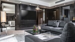 Uma sala de estar moderna com uma televisão de tela plana grande, sofás cinzas, uma mesa de centro de vidro e um vaso decorativo.