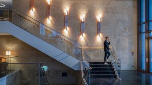 Um interior moderno com escada de vidro, guarda-corpos de metal e luminárias fixadas na parede.