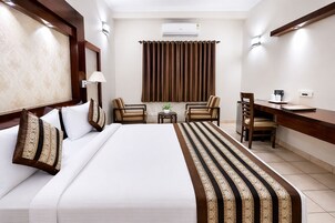 Quarto de hotel com uma cama, duas cadeiras, uma escrivaninha, uma mesa pequena e um ar condicionado.