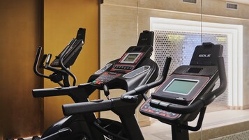 Uma fileira de bicicletas ergométricas com mostradores digitais e painéis de controle, provavelmente em uma academia ou centro de ginástica.