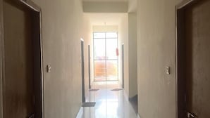Um corredor comprido e estreito com piso de azulejos que leva a um quarto claro, com uma grande janela.