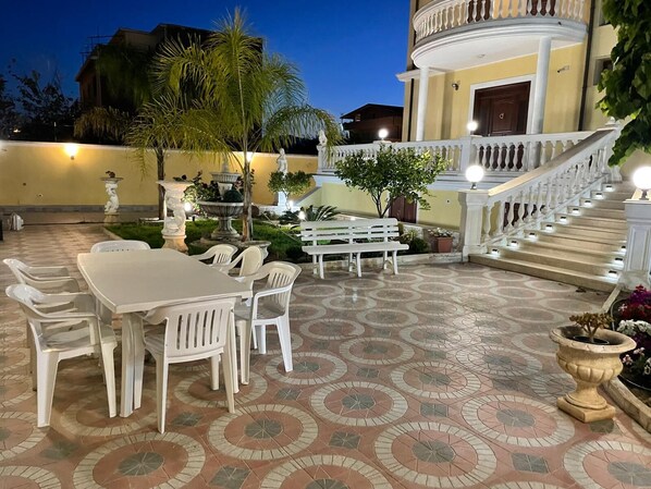 Uma área de pátio ao ar livre com uma mesa de jantar, cadeiras, escadas e plantas decorativas.